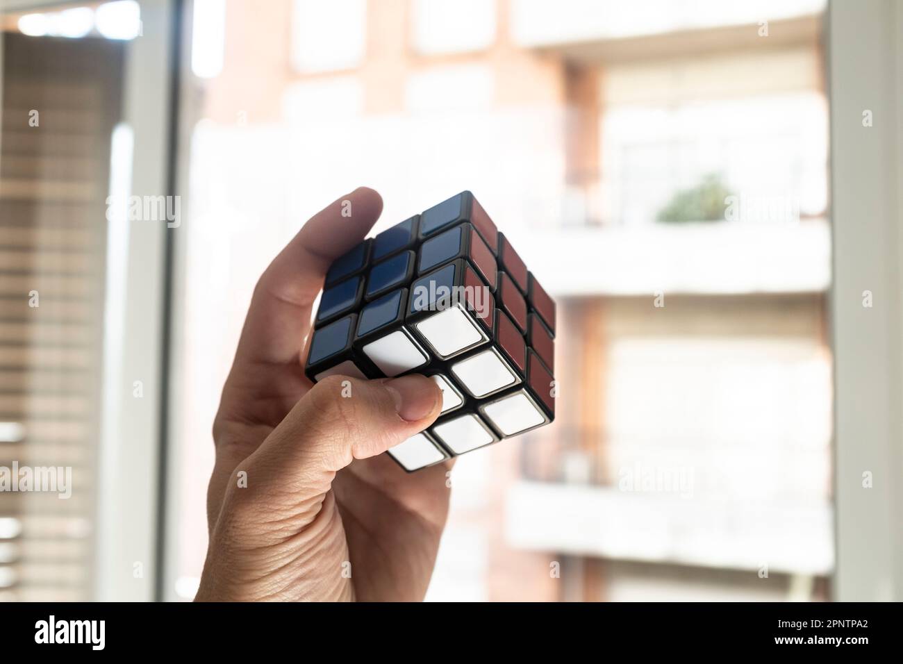 Left hand hanging a perfect done Rubik cube puzzle in a domestic house ...