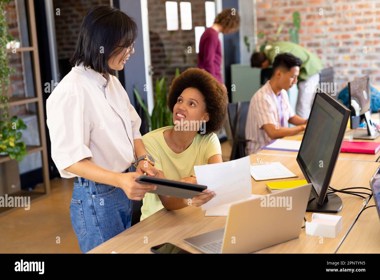 Two happy diverse female creative colleagues using tablet and ...
