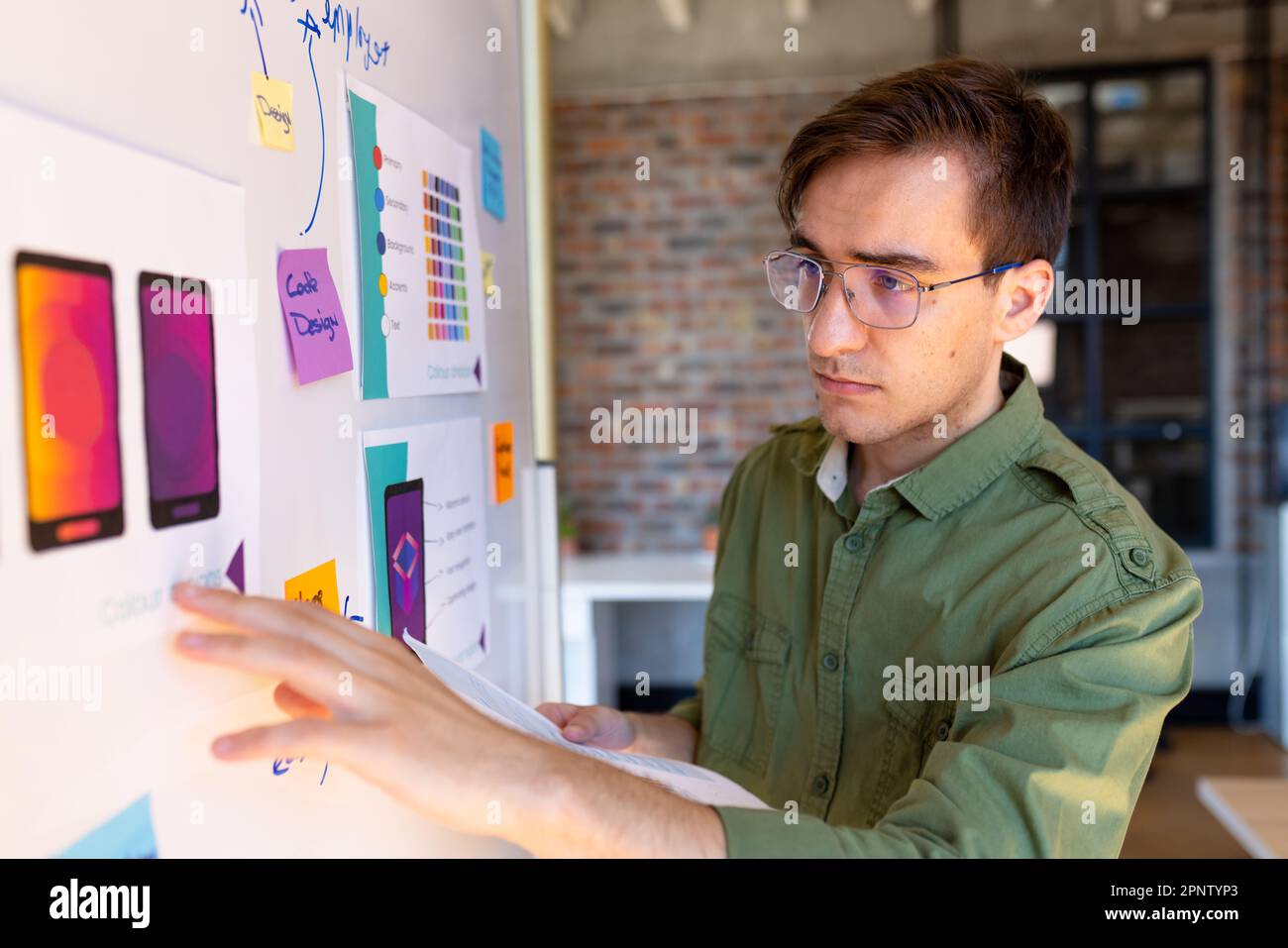 Thoughtful caucasian male designer looking at design mock ups and notes ...