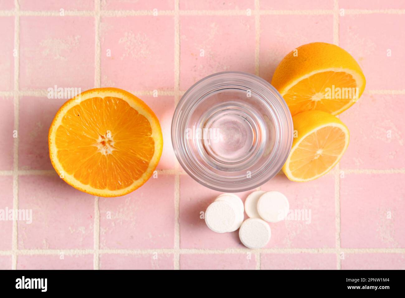 Glass of water, vitamin C effervescent tablets and fruits on pink tiled ...