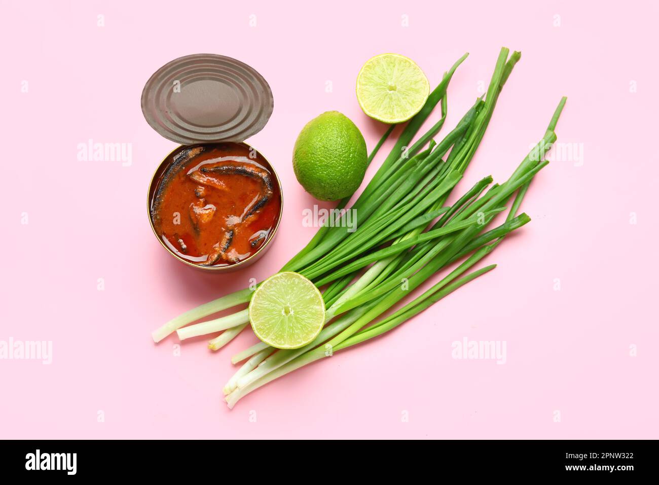 Opened tin can with fish in tomato sauce, lime and scallions on pink ...