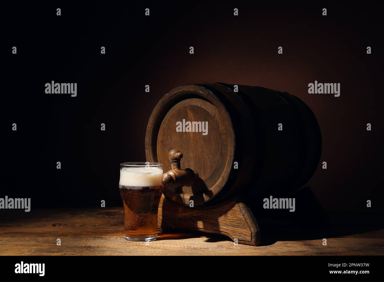Wooden barrel and glass of cold beer on table against dark background ...