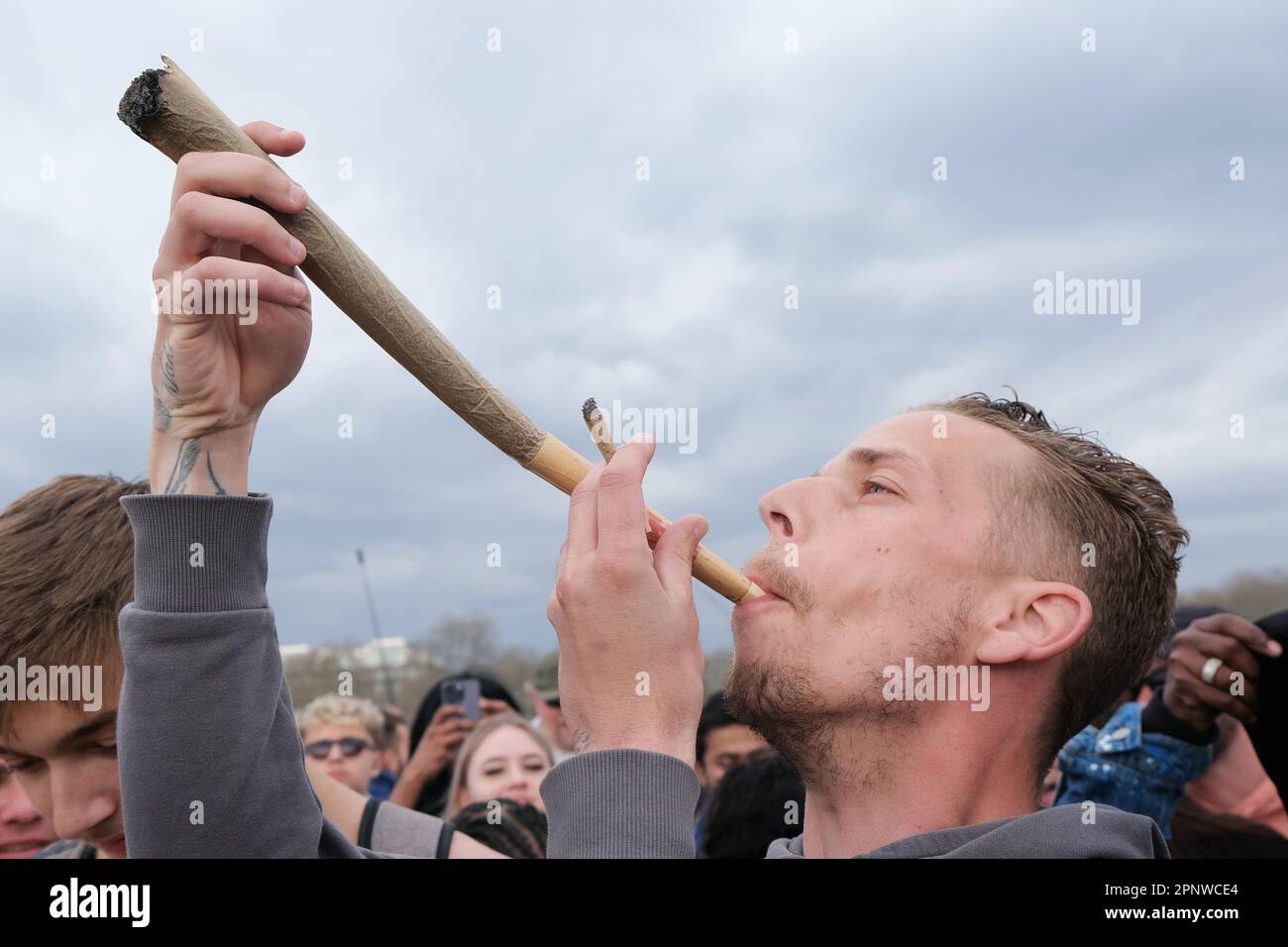 London, UK. 20th April, 2023. A man smokes an oversized spliff - with a ...