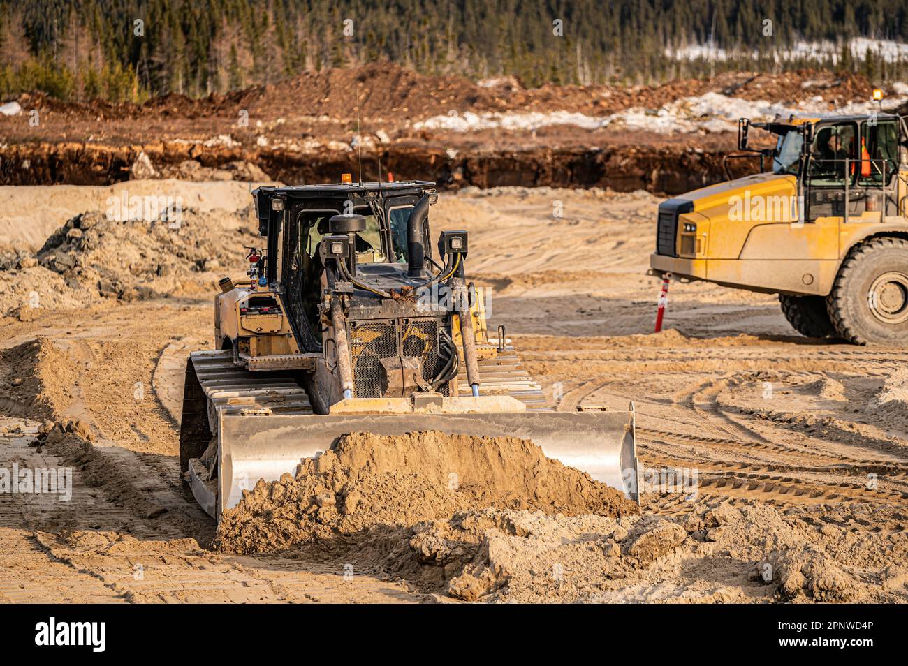 Bulldozer pushing sand on the bottom of an excavation in boreal forest ...