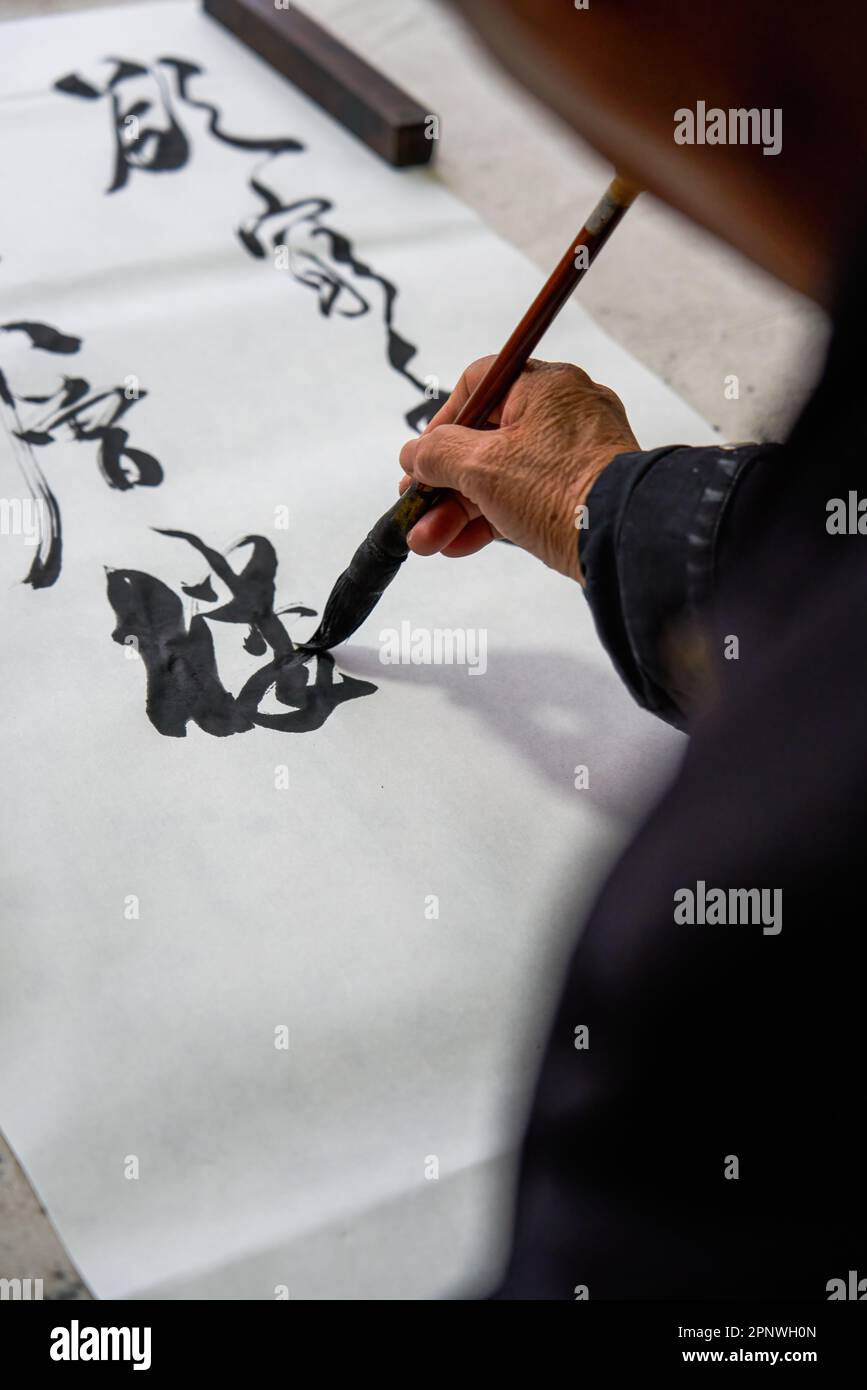 An old Chinese calligrapher is writing brush characters, creating ...