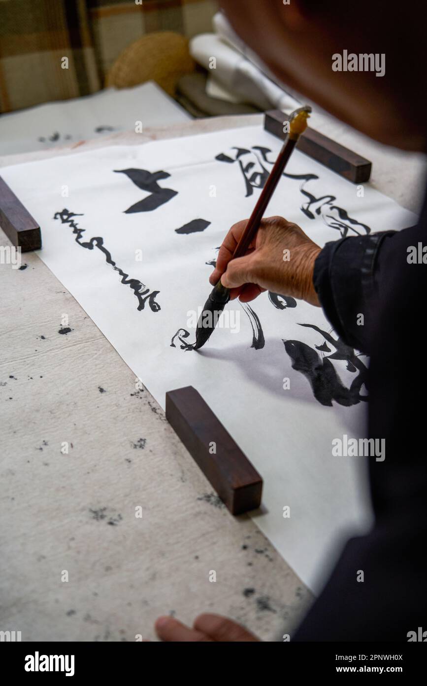 An old Chinese calligrapher is writing brush characters, creating ...