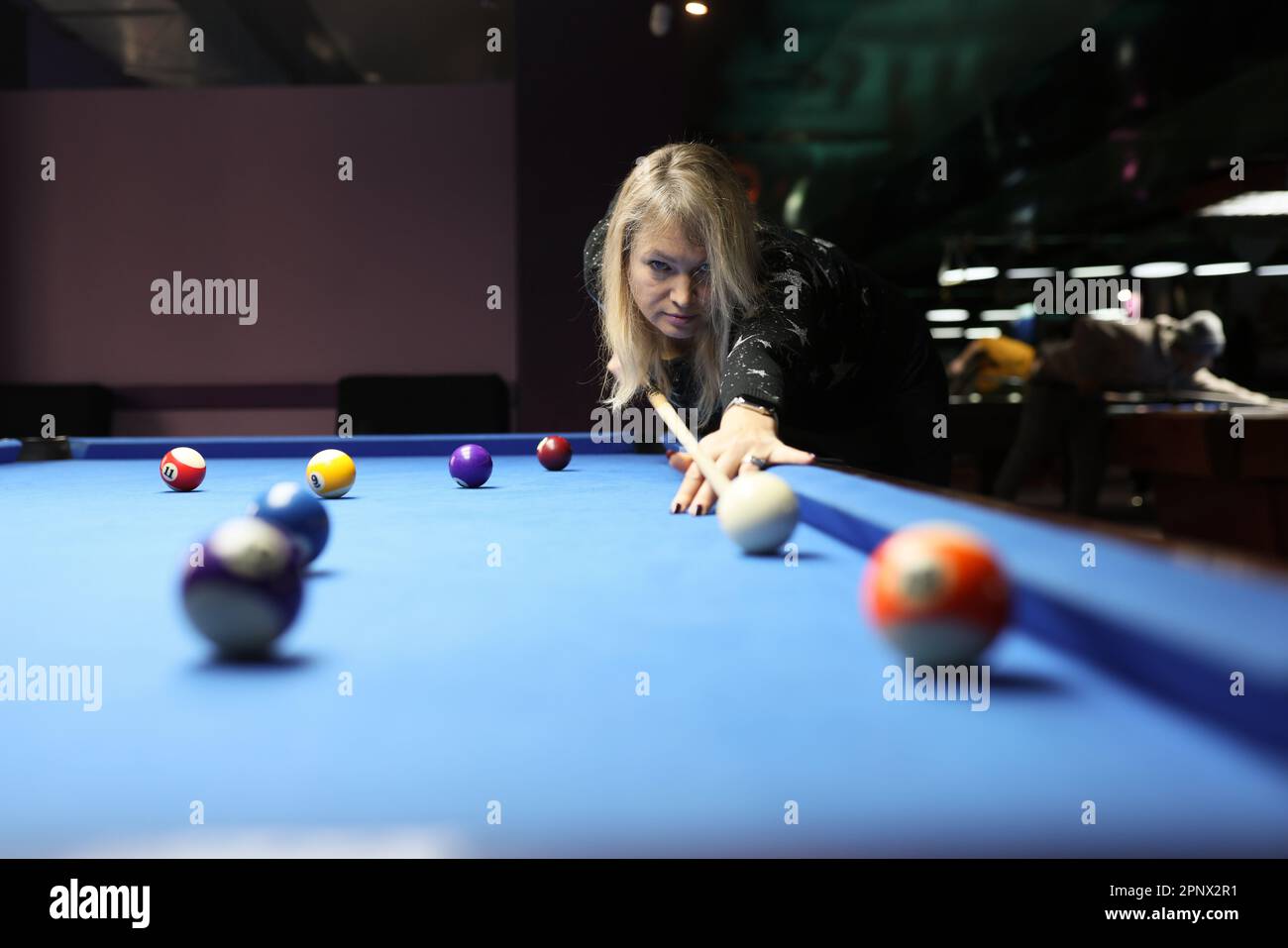 Focused woman hits white ball leaning above blue pool table Stock Photo ...
