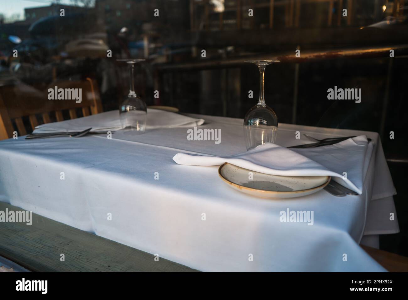Empty restaurant dining room, lights off. White table cloth, wooden ...