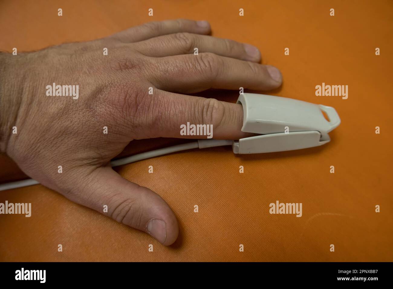 Hand with pulse oximeter on orange background Stock Photo - Alamy