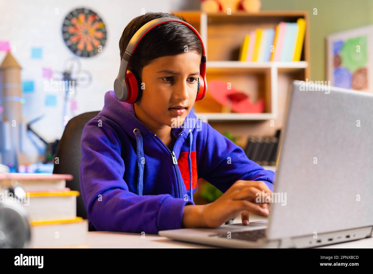 Indian teenager kid with headphones working laptop on study table at ...