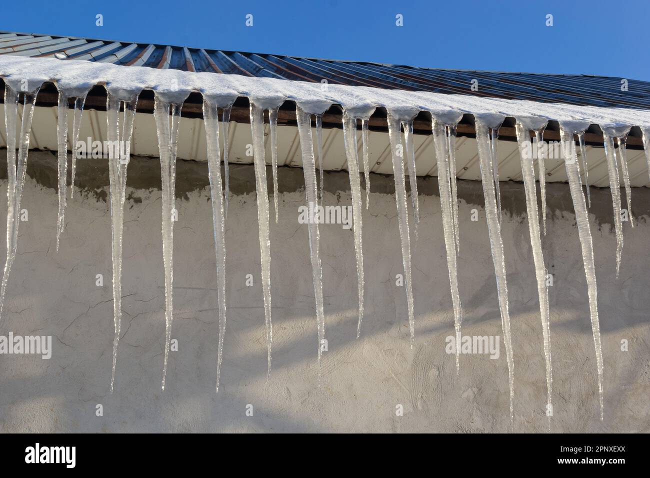 Sharp icicles and melted snow hanging from eaves of roof. Beautiful ...
