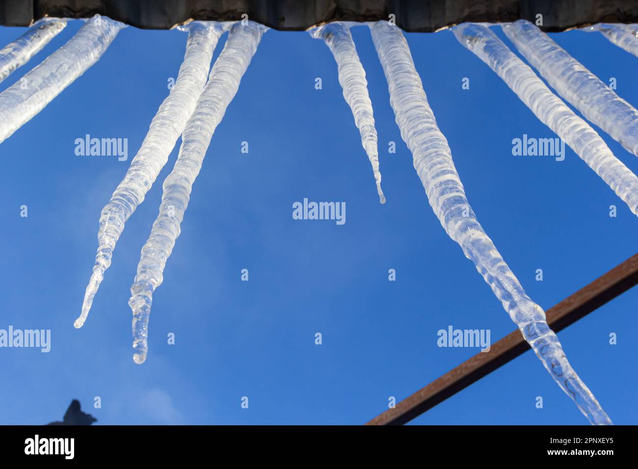 Sharp icicles and melted snow hanging from the eaves of the roof ...