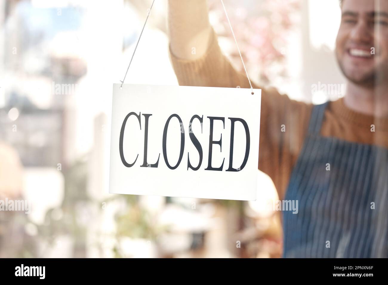 Closed, sign and happy man at shop, store and notice of retail closing ...