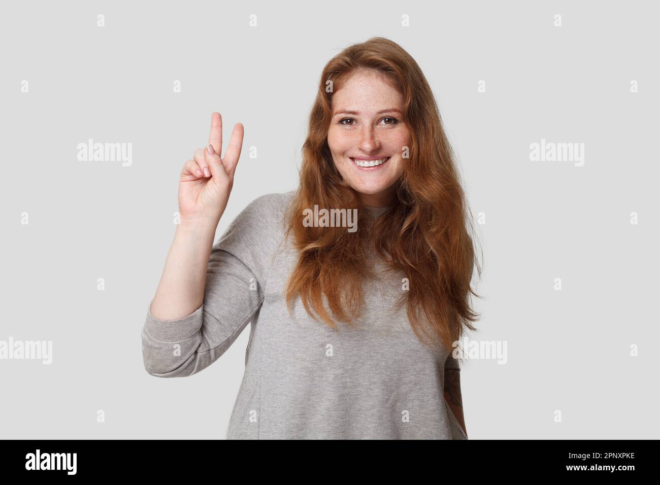 Cute friendly positive woman showing two finger on white background ...