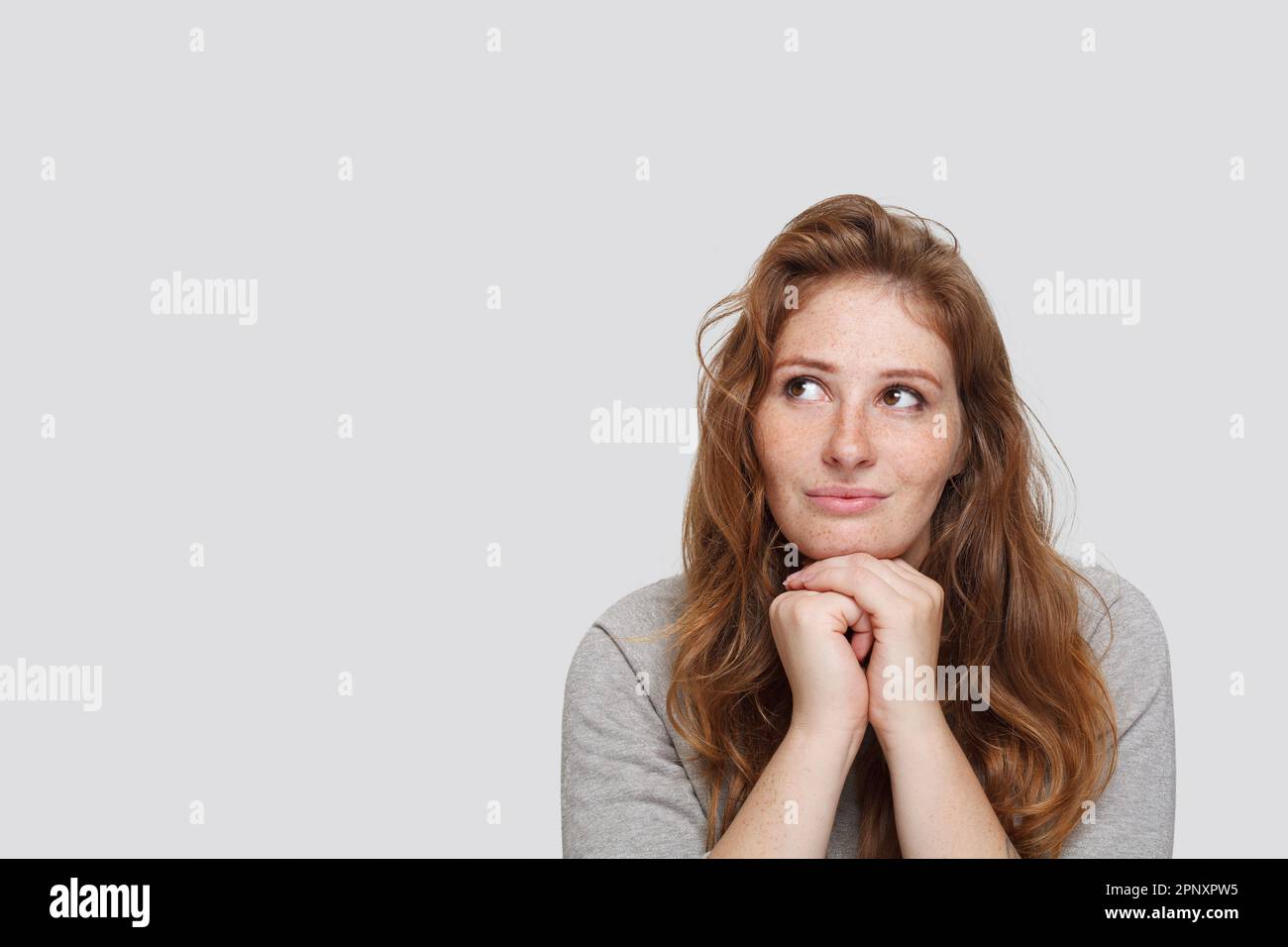 Portrait of pretty thinking woman with long wavy ginger hair on white ...