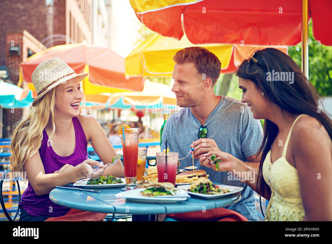 Enjoying a meal with friends. three young friends sitting at an outdoor ...