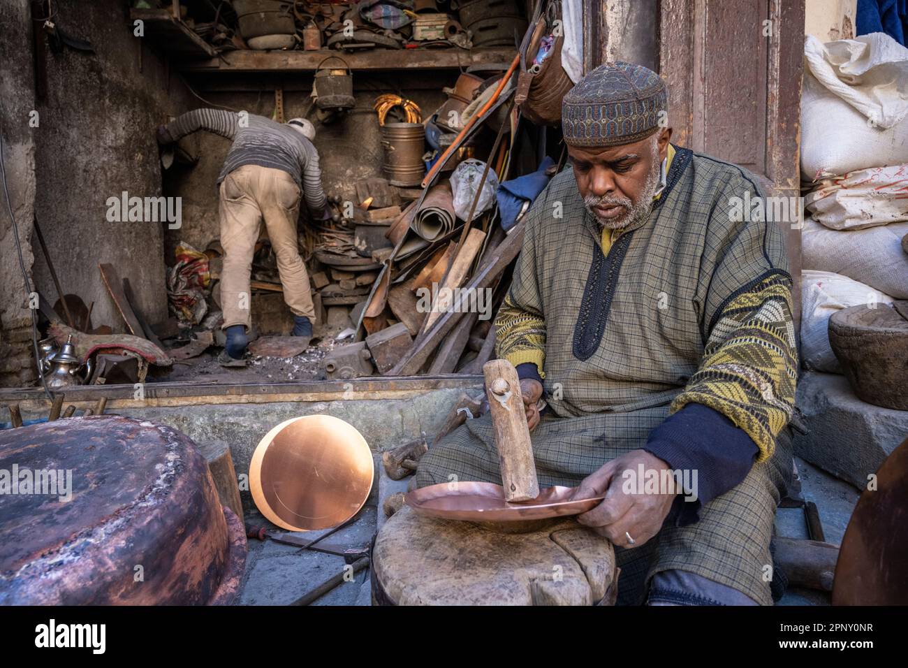 Craftsman making a copper plate with a wooden hammer, in a small street ...