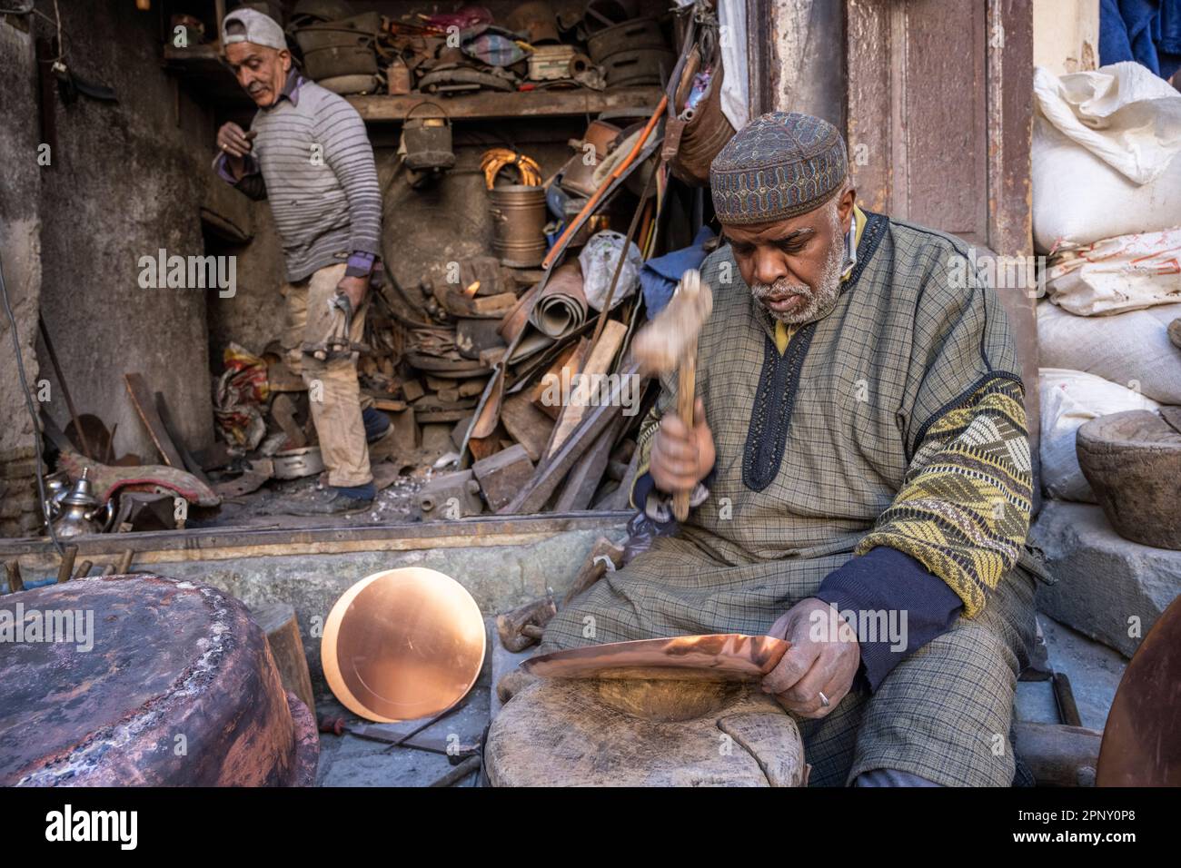 Craftsman making a copper plate with a wooden hammer, in a small street ...