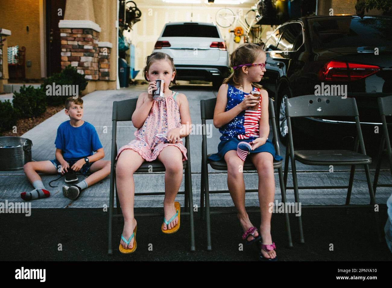 Girls and boy sitting in home driveway drinking soda in summer Stock ...