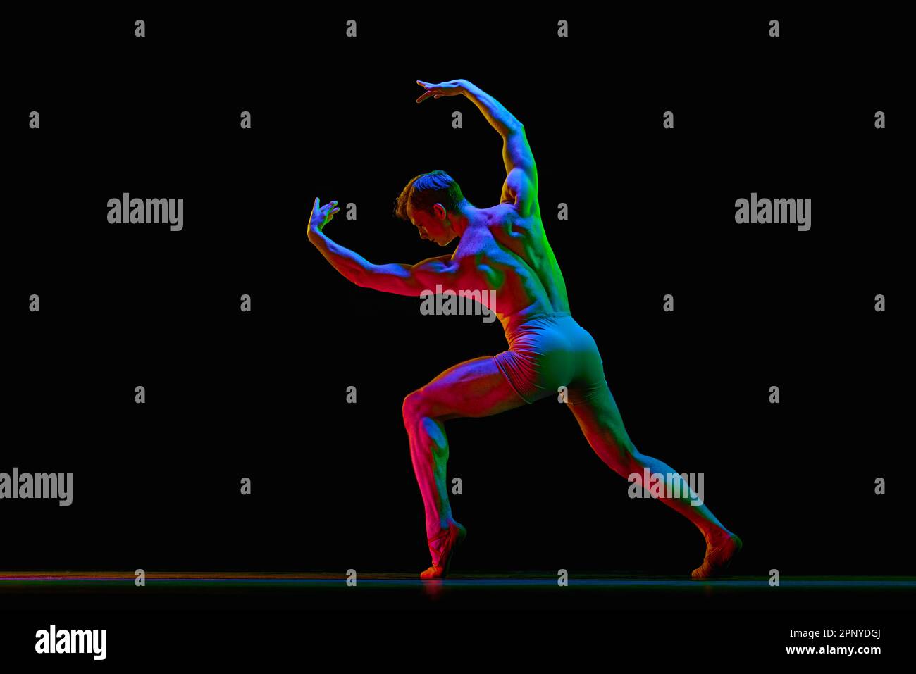 Athletic ballet dancer in a perfect shape performing over dark studio ...