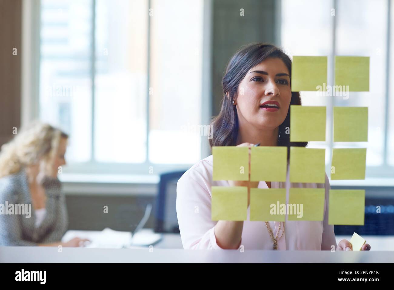 Streamlining ideas. a businesswoman reading adhesive notes on a glass ...