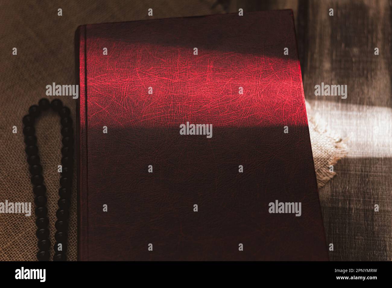 A hard ray of sun falls on an old red book. Sunbeam in the dark, on a ...