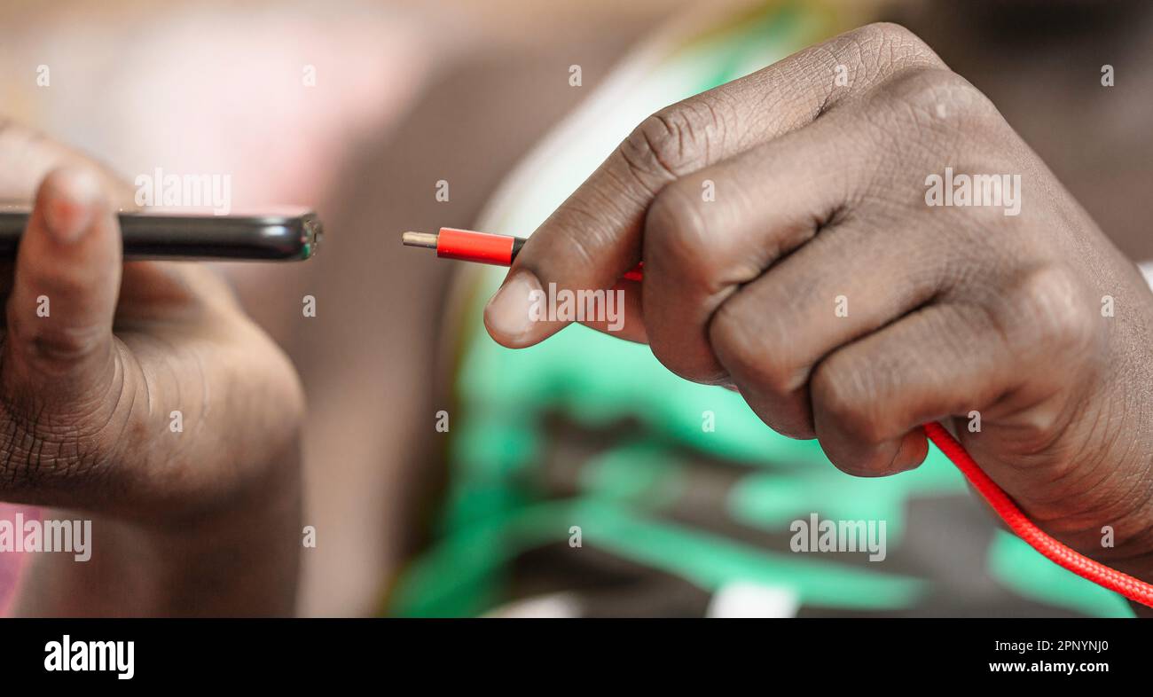 A black hand connects a USB cable to a mobile phone's charging port in ...