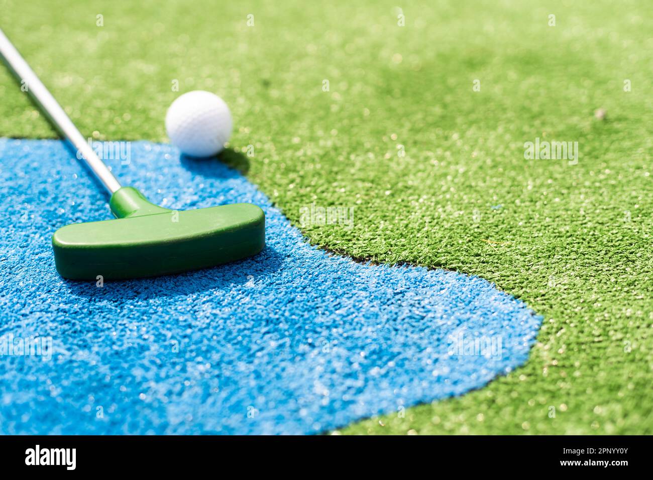 Mini-golf clubs and balls of different colors laid on artificial grass ...