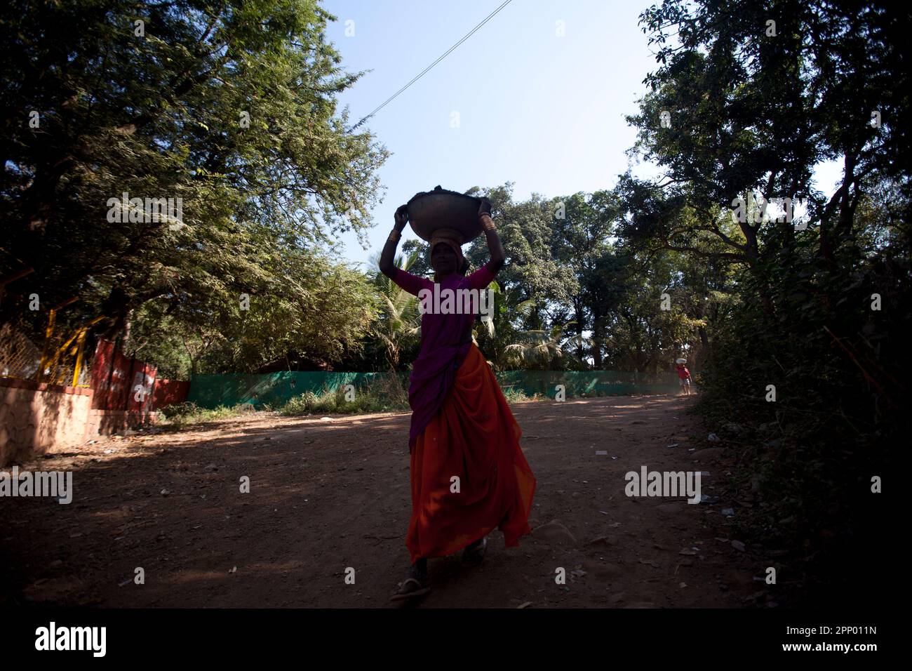A lady construction worker, labour walking with cement on her head ...