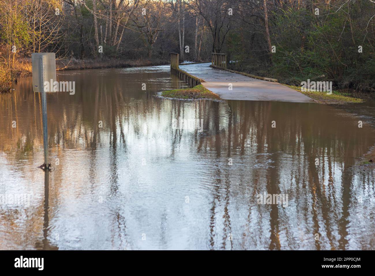 A walkway and sign are partially submerged from a nearby creek flooding ...