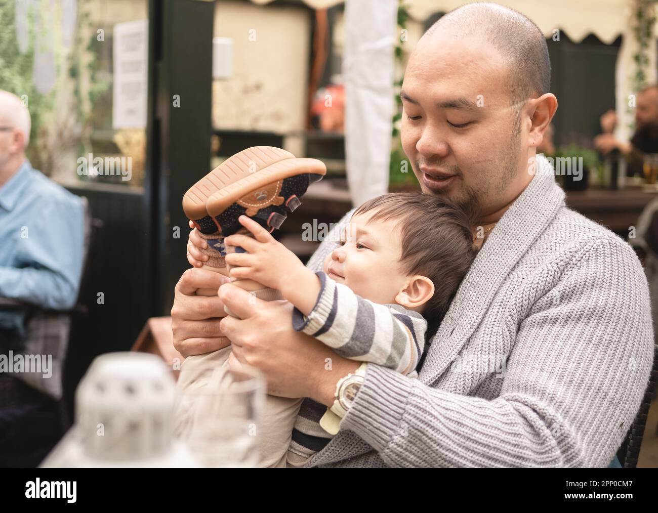 Flexible male infant holding his own legs sitting on his dad's legs ...