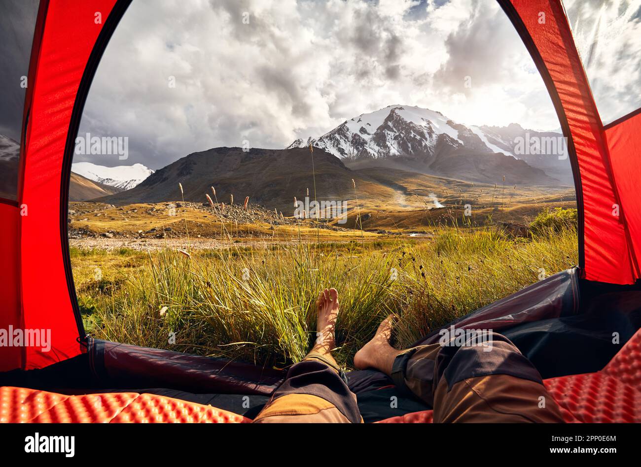 View from inside a tent and hikers legs to the mountains valley with ...