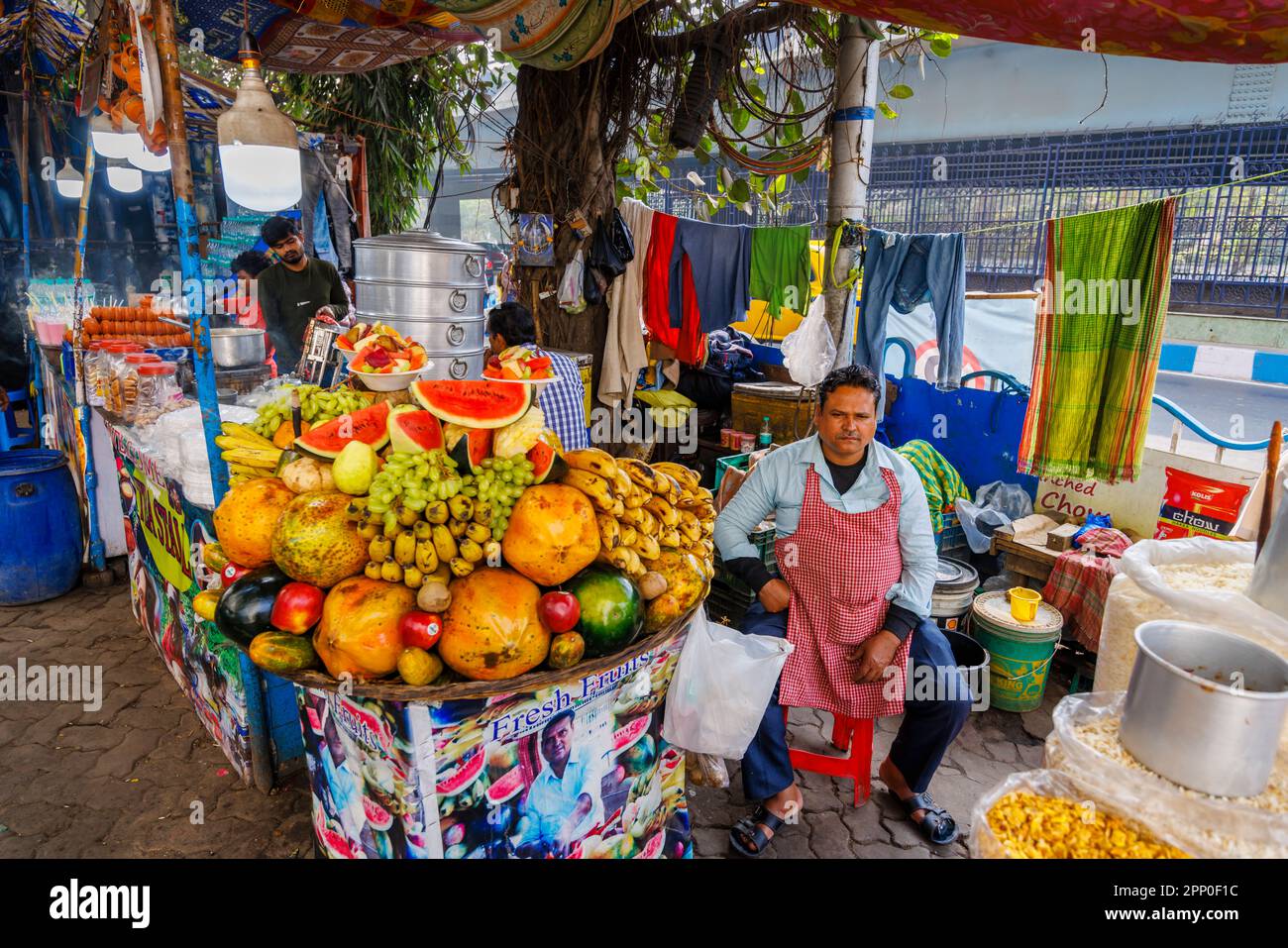 Roadside stall selling fruit and seated local male stallholder seller ...