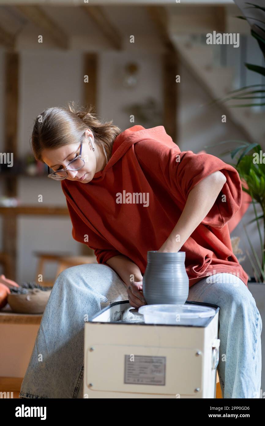Creative artisan woman teacher of ceramic courses shaping jug sits near ...