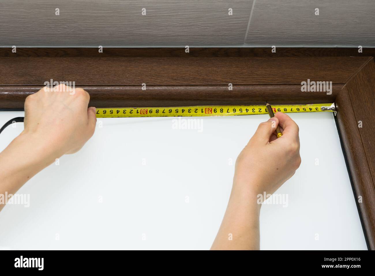 View of a man measuring a brown plastic window with a tape measure ...