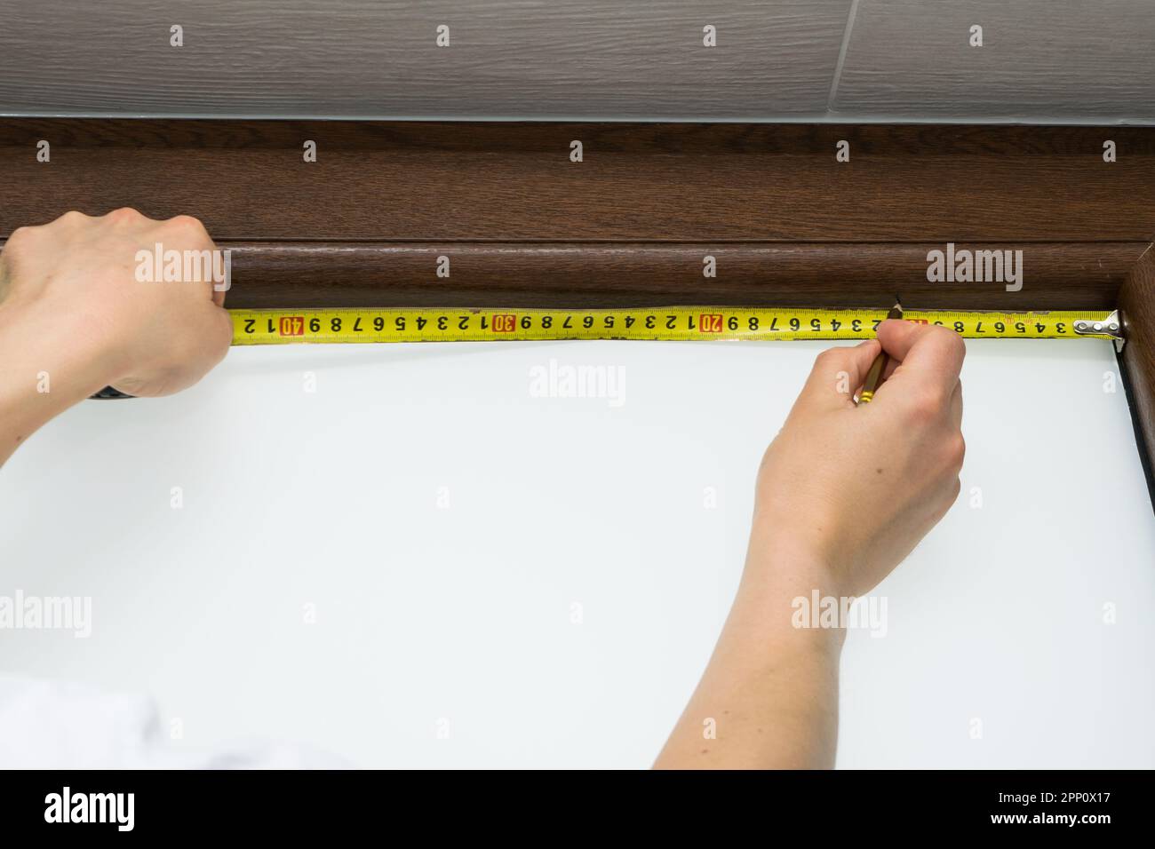 View of a man measuring a brown plastic window with a tape measure ...