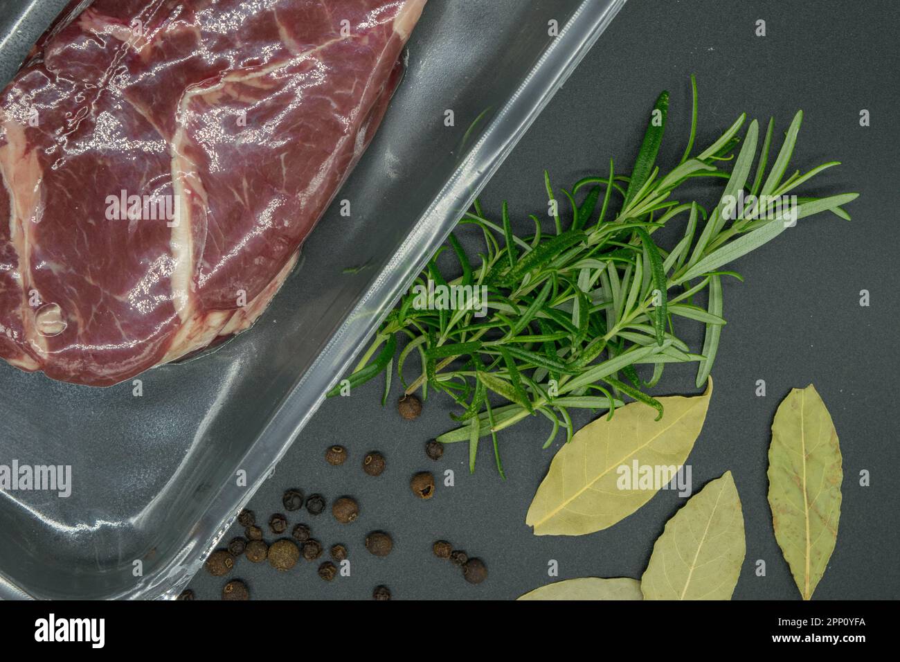 Beef steak, view of fresh beef in a foil wrapper on a dark background with rosemary, black ...