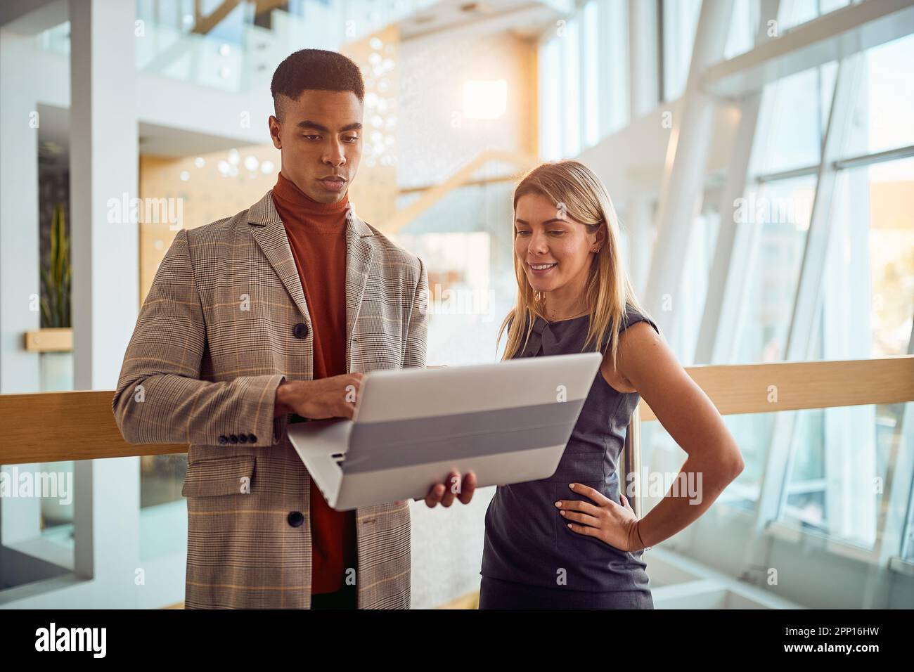 Two young colleagues are watching a laptop content while standing in a pleasant atmosphere in ...