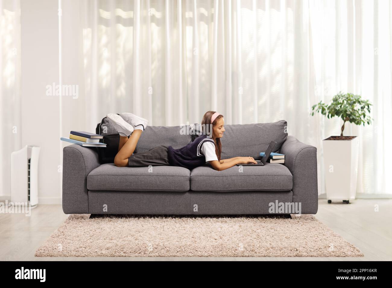 Child laying on a sofa and using a laptop computer at home in a living ...