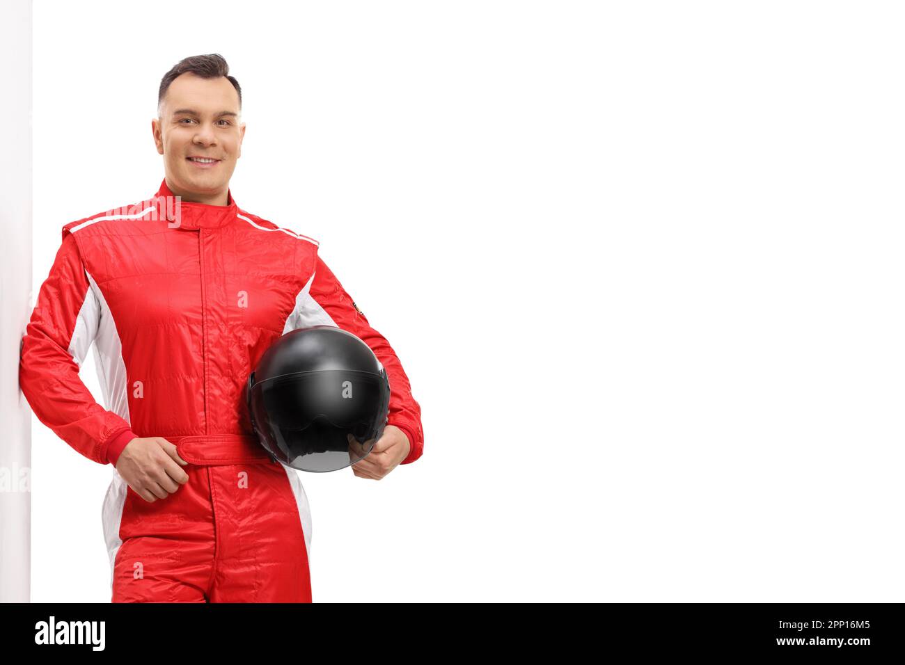 Racer in a red suit leaning on a wall and holding a black helmet ...