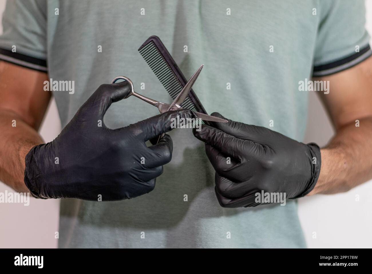 A barber's black-gloved hands holding a pair of scissors to a comb ...