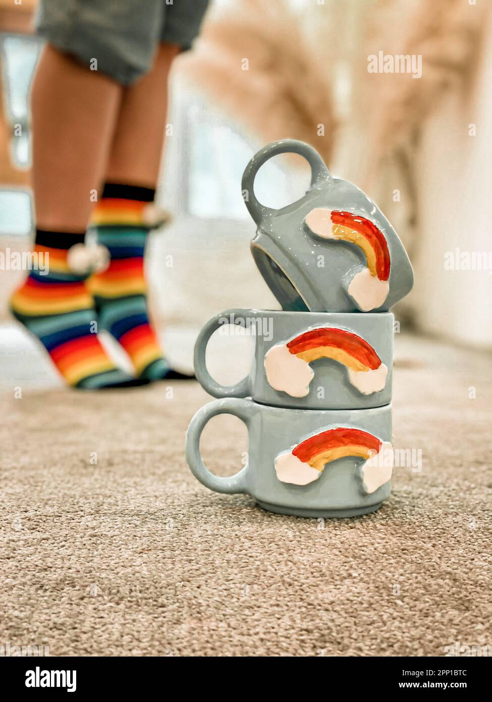 The ceramic mugs with rainbow designs on the background of a kid's legs ...
