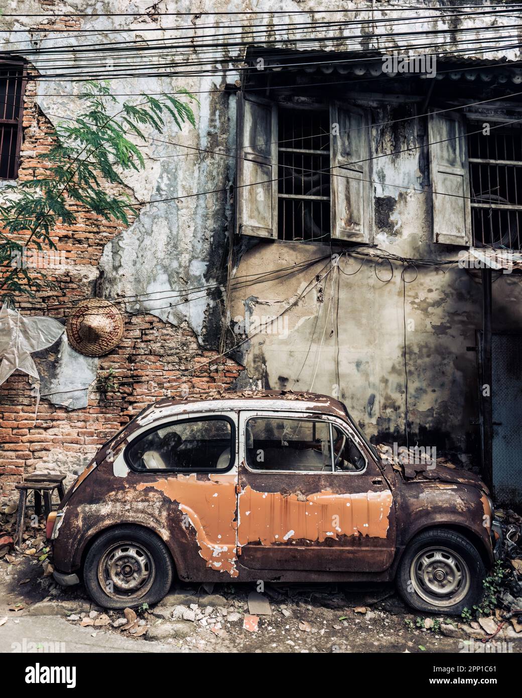 An old, rusted Fiat 500 parked in the driveway of a derelict building ...