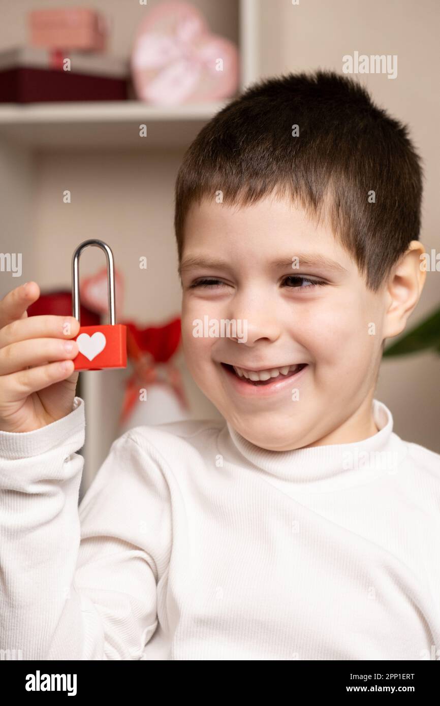 A 5 year old cute boy holds a lock with heart and looks at it ...