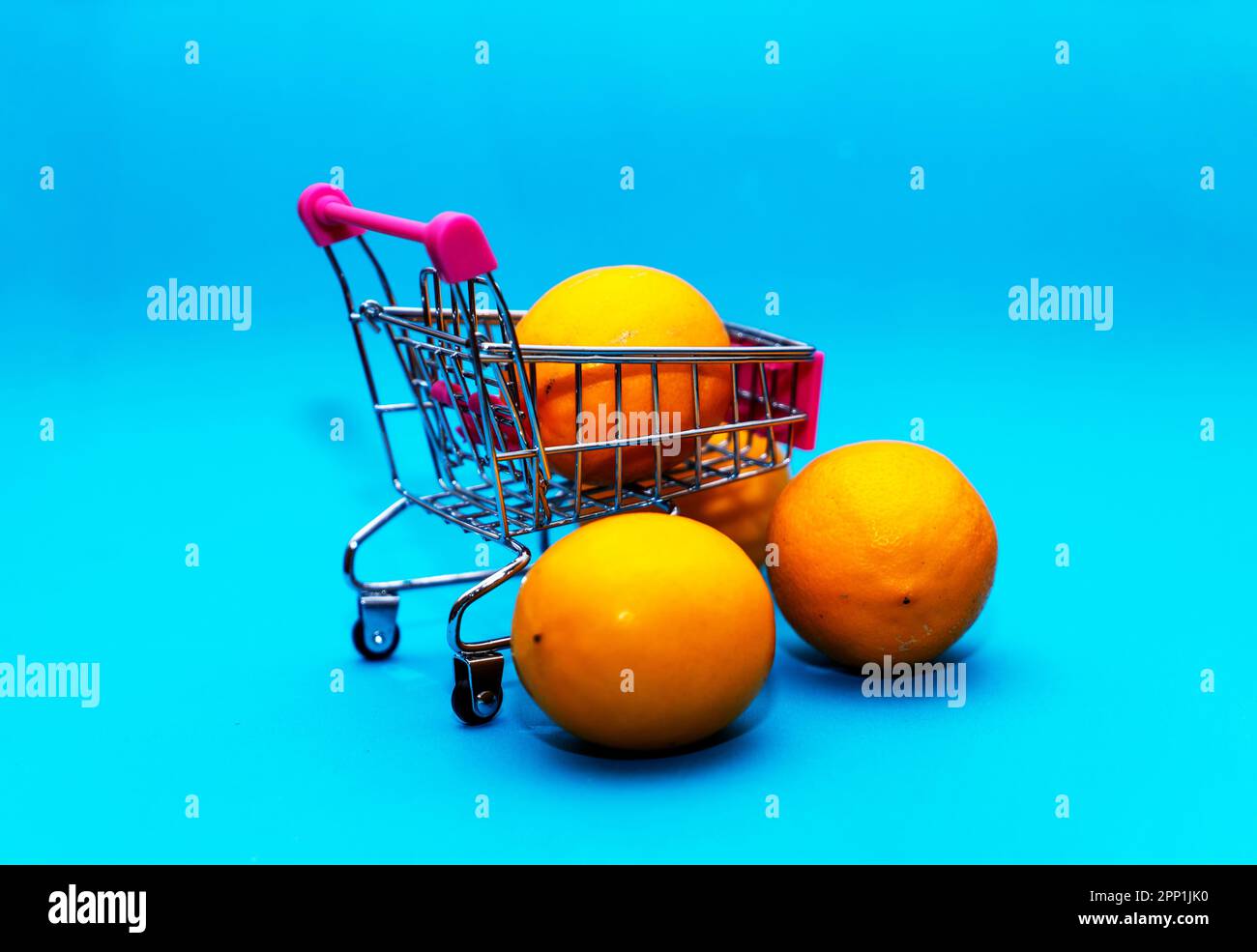 Oranges in an iron grocery cart on a blue background. Business and ...