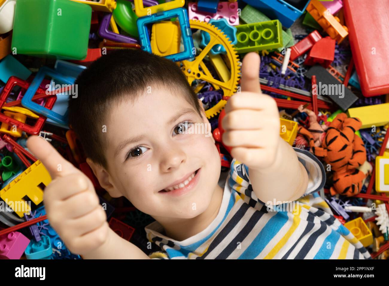 Happy 5 year old boy showing thumbs up lying among toys, top view Stock ...