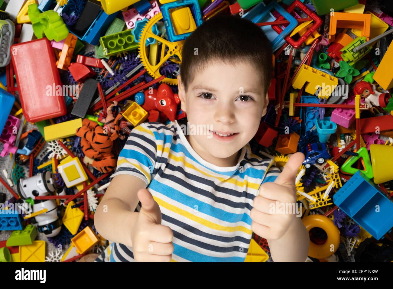 Happy 5 year old boy showing thumbs up lying among toys, top view Stock ...