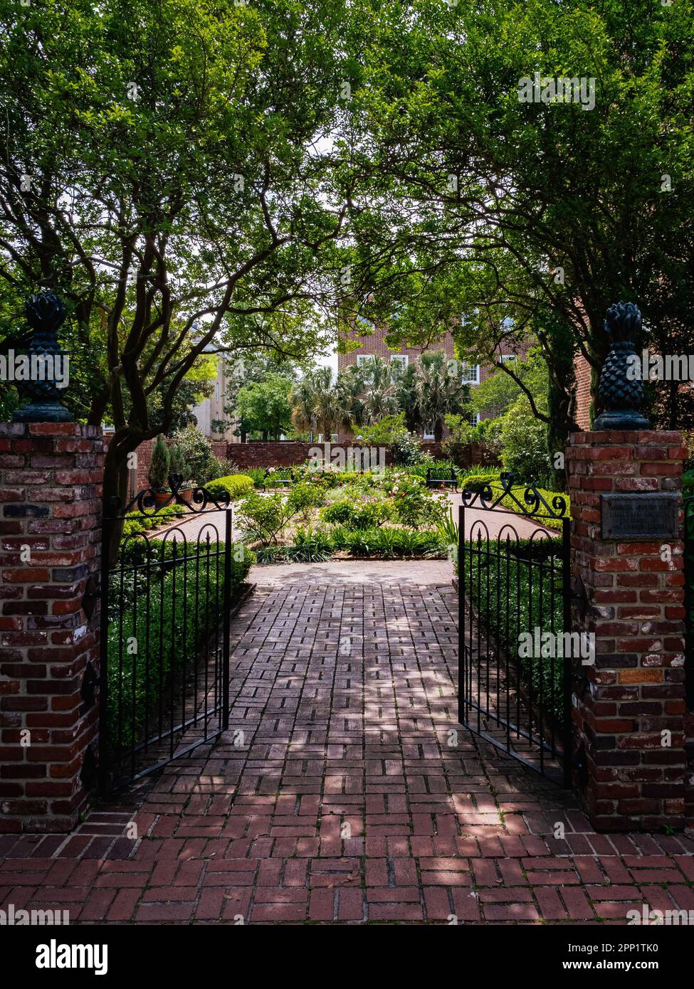 A pathway made of red bricks with ornate, black iron gates. The ...