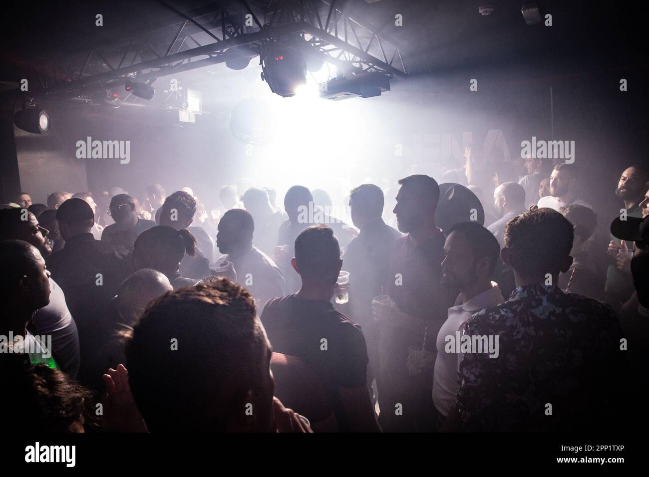 silhouettes of people on the dancefloor of a smokey club with bright ...
