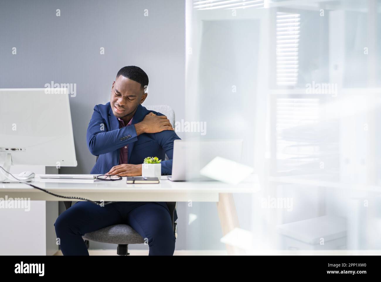 Young Businessman Having Shoulder Pain While Working At Computer Desk ...